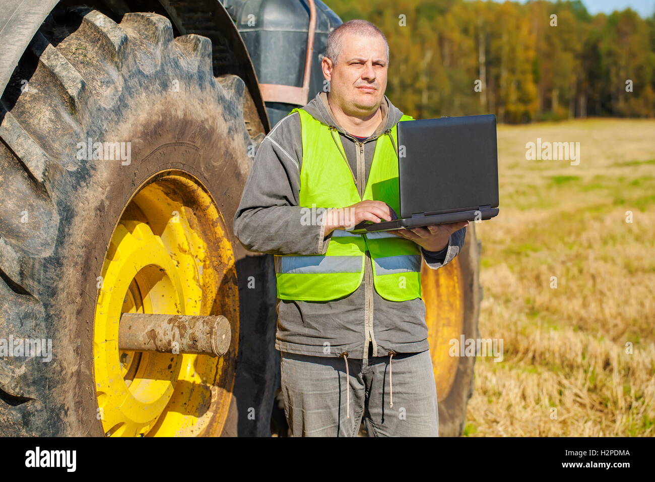 Farmer with computer near the tractor on field Stock Photo - Alamy