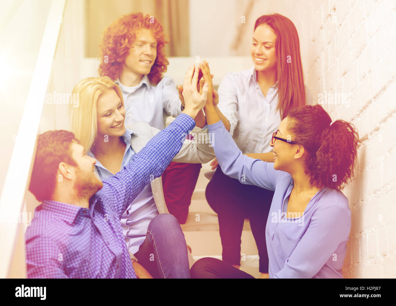 team doing high five gesture sitting on staircase Stock Photo - Alamy