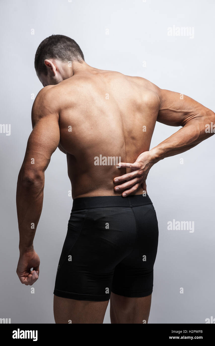 Male athlete with pain in his lower back, isolated in grey Stock Photo ...
