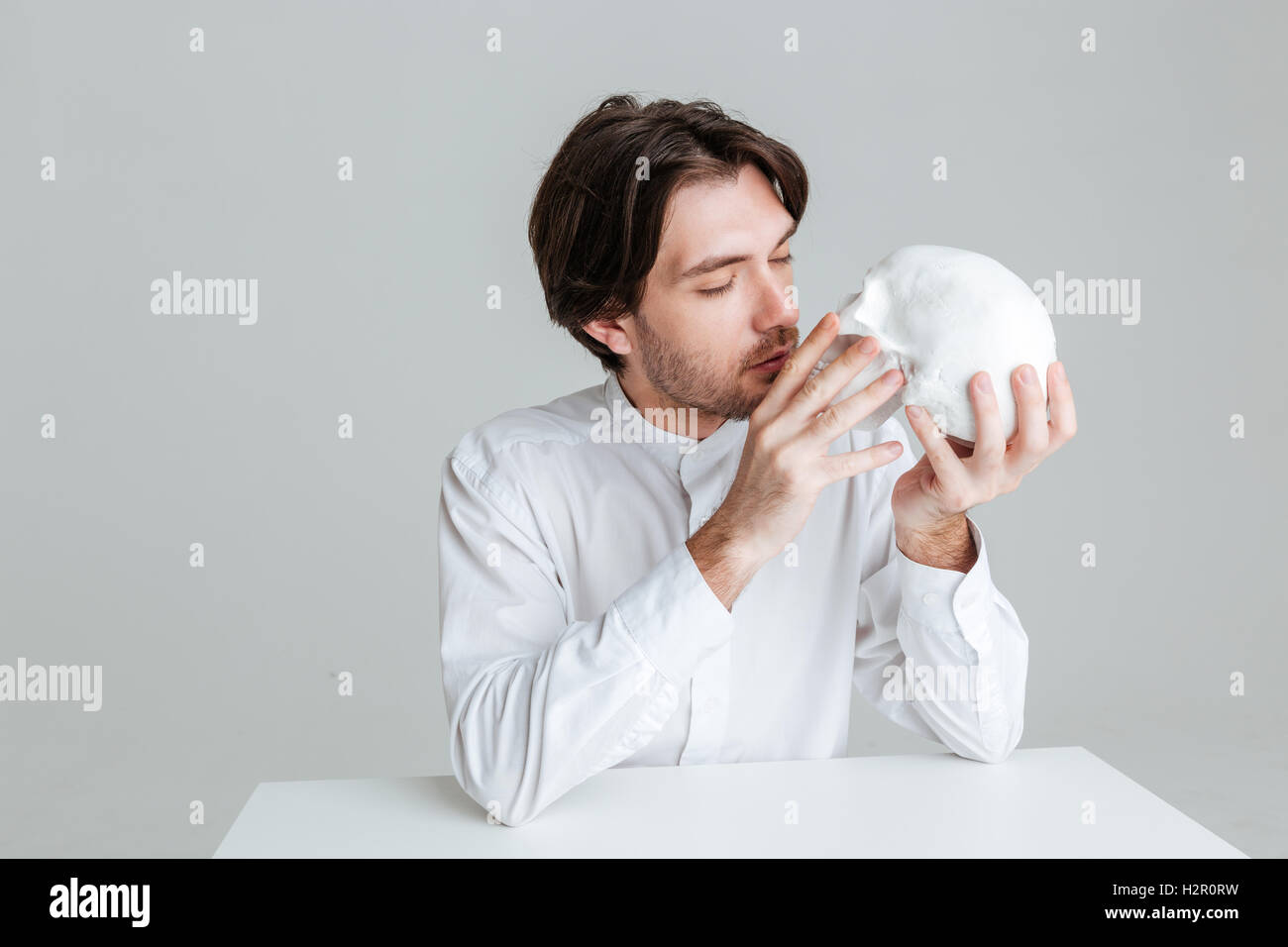 Young brunette man kissing fake skull isolated on the gray background ...