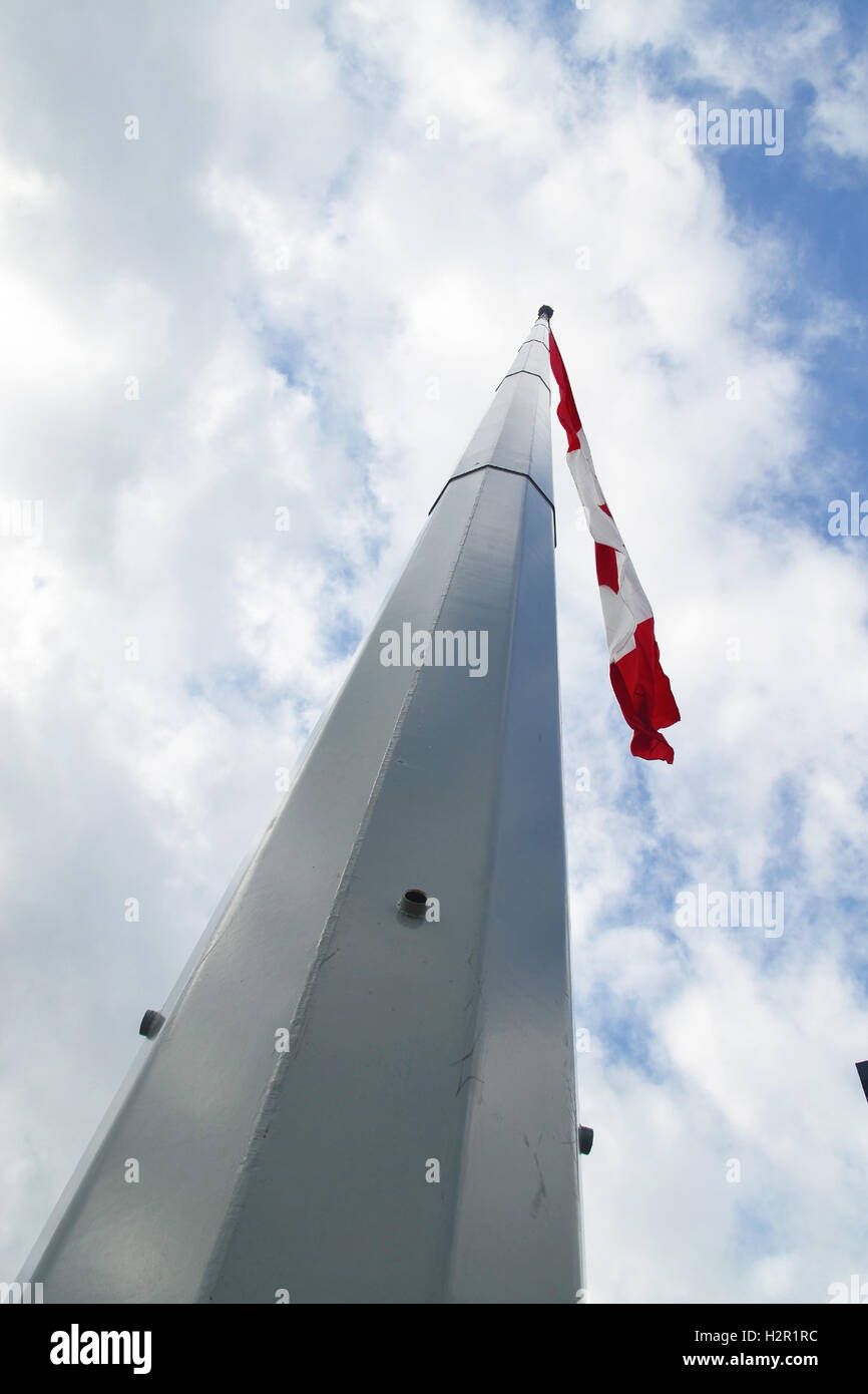 A very tall steel flag pole with a Canadian flag flying in the wind ...