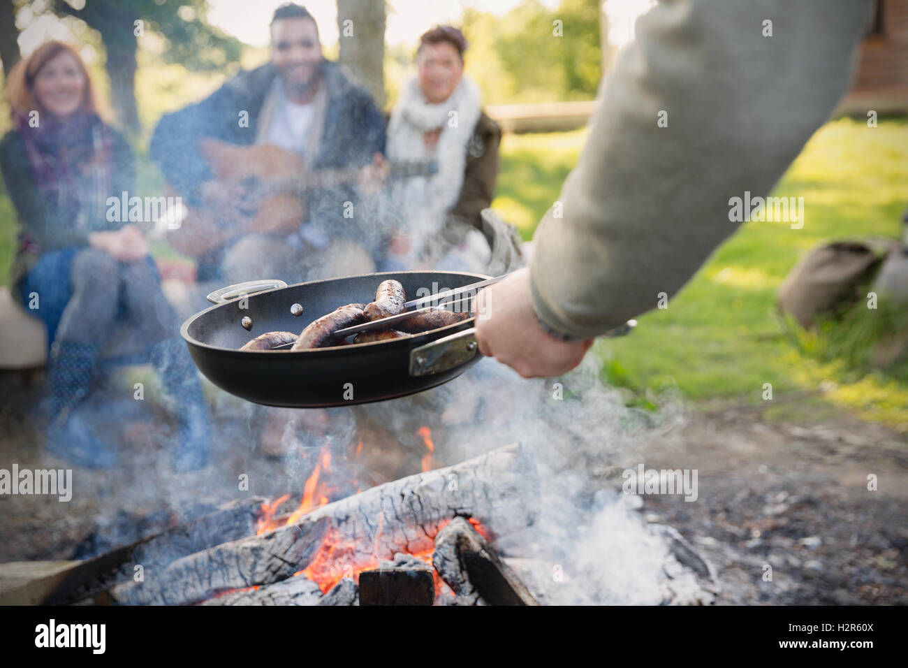 Man cooking hot dogs over campfire for friends Stock Photo - Alamy