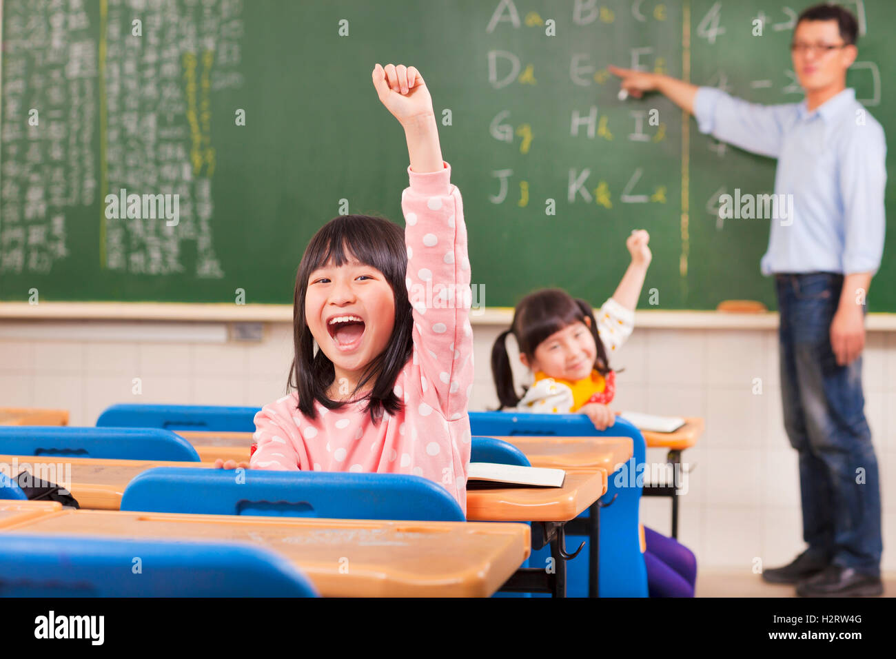 happy pupils raising hands during the lesson Stock Photo - Alamy