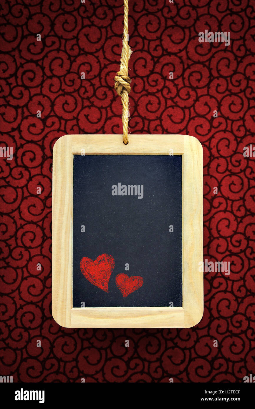 Writing slate with hearts hanged by a rope over a red background with ...