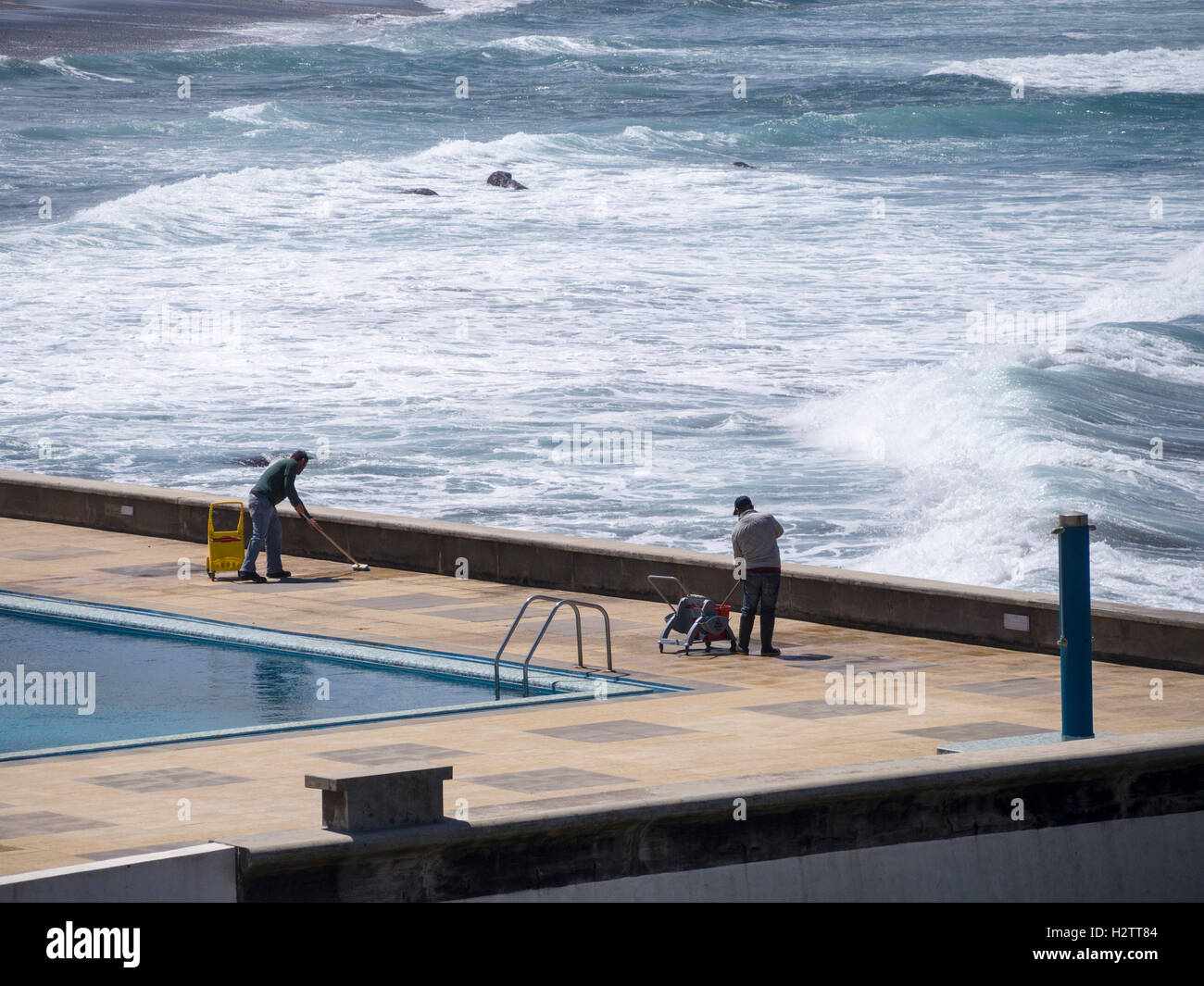 Cleaning Up the Pool. Two workmen scrub the deck of an oceanside ...