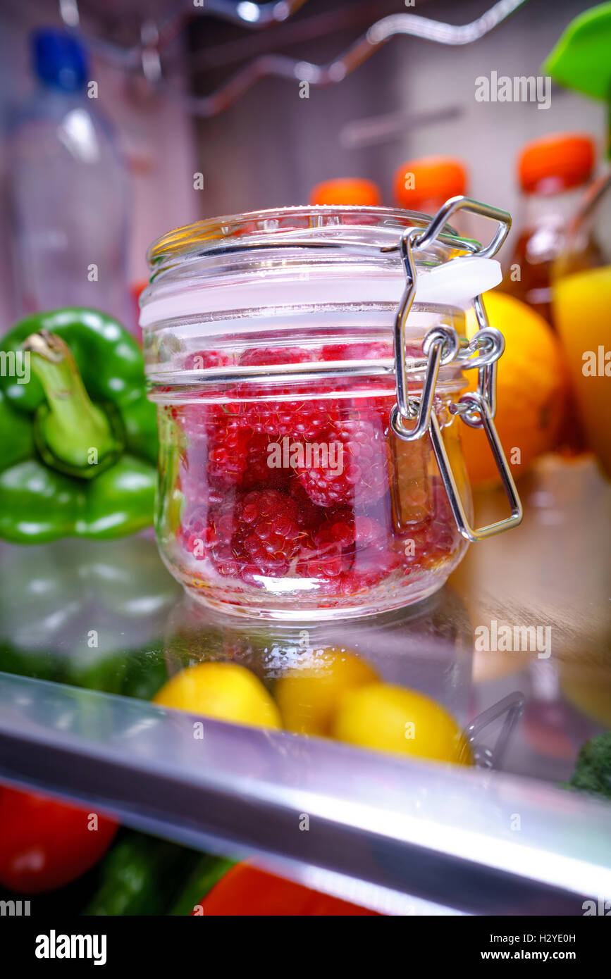 Fresh raspberries in a glass jar on a shelf open refrigerator. Healthy ...