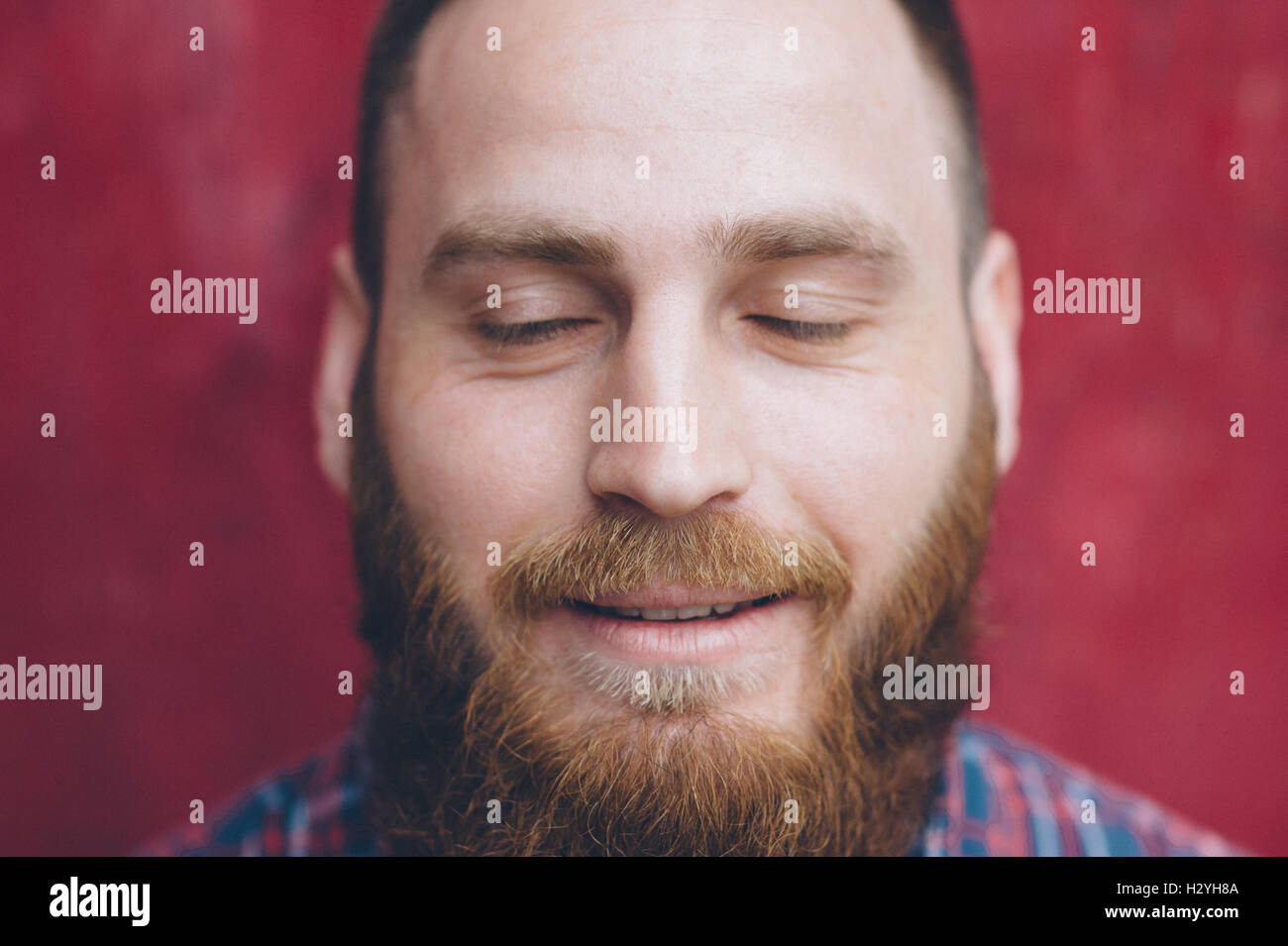 bearded young man on a background of a red wall dreaming with closed ...