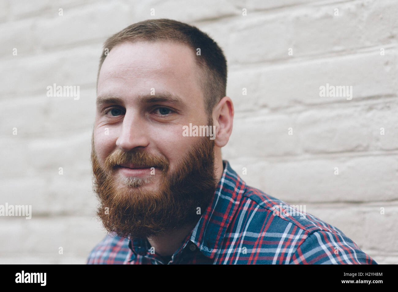 portrait of a smiling man with a beard in front of the white brick wall ...