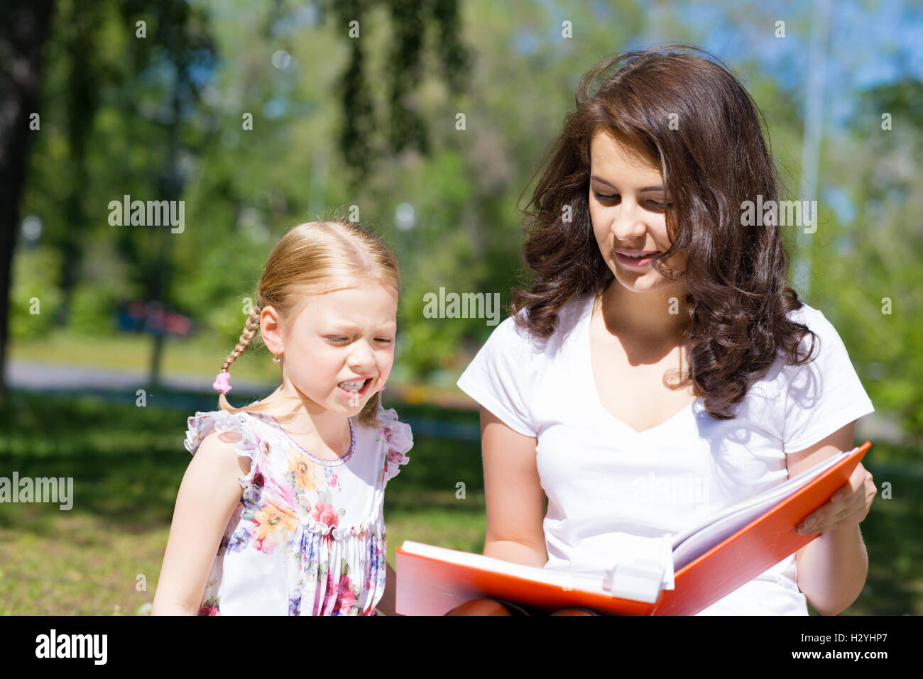 girl and a young woman reading a book together Stock Photo - Alamy