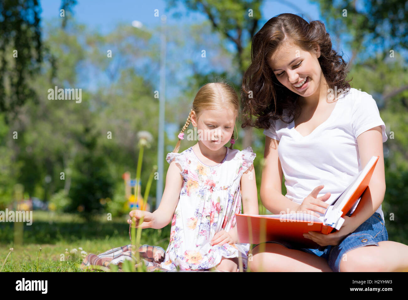 girl and a young woman reading a book together Stock Photo - Alamy