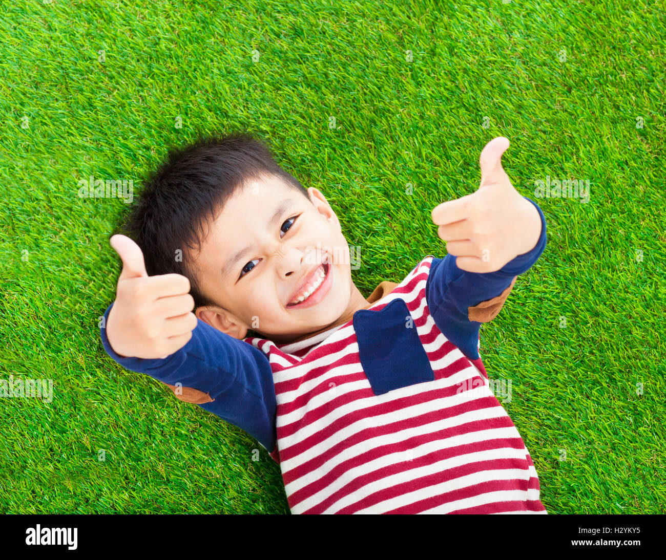 smiling kid lying and thumb up on a meadow Stock Photo - Alamy
