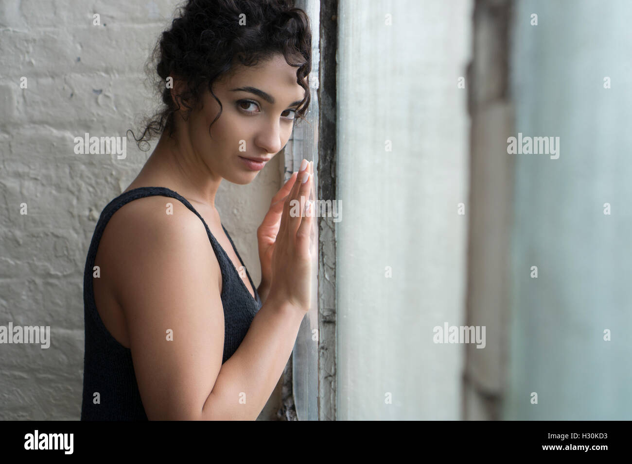Beautiful young woman leaning against the window Stock Photo - Alamy