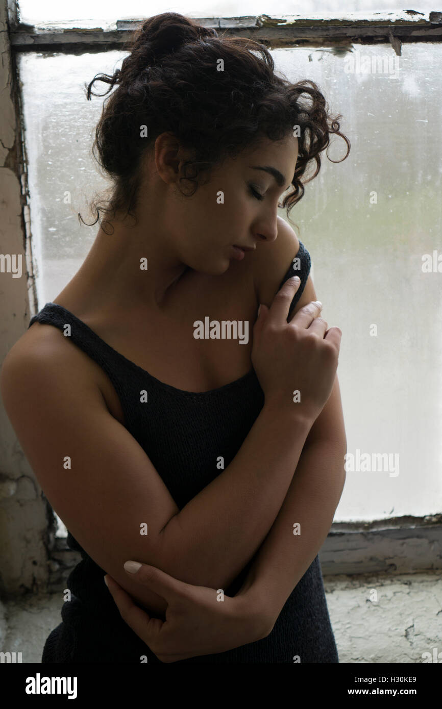 Beautiful young woman standing by the window Stock Photo - Alamy