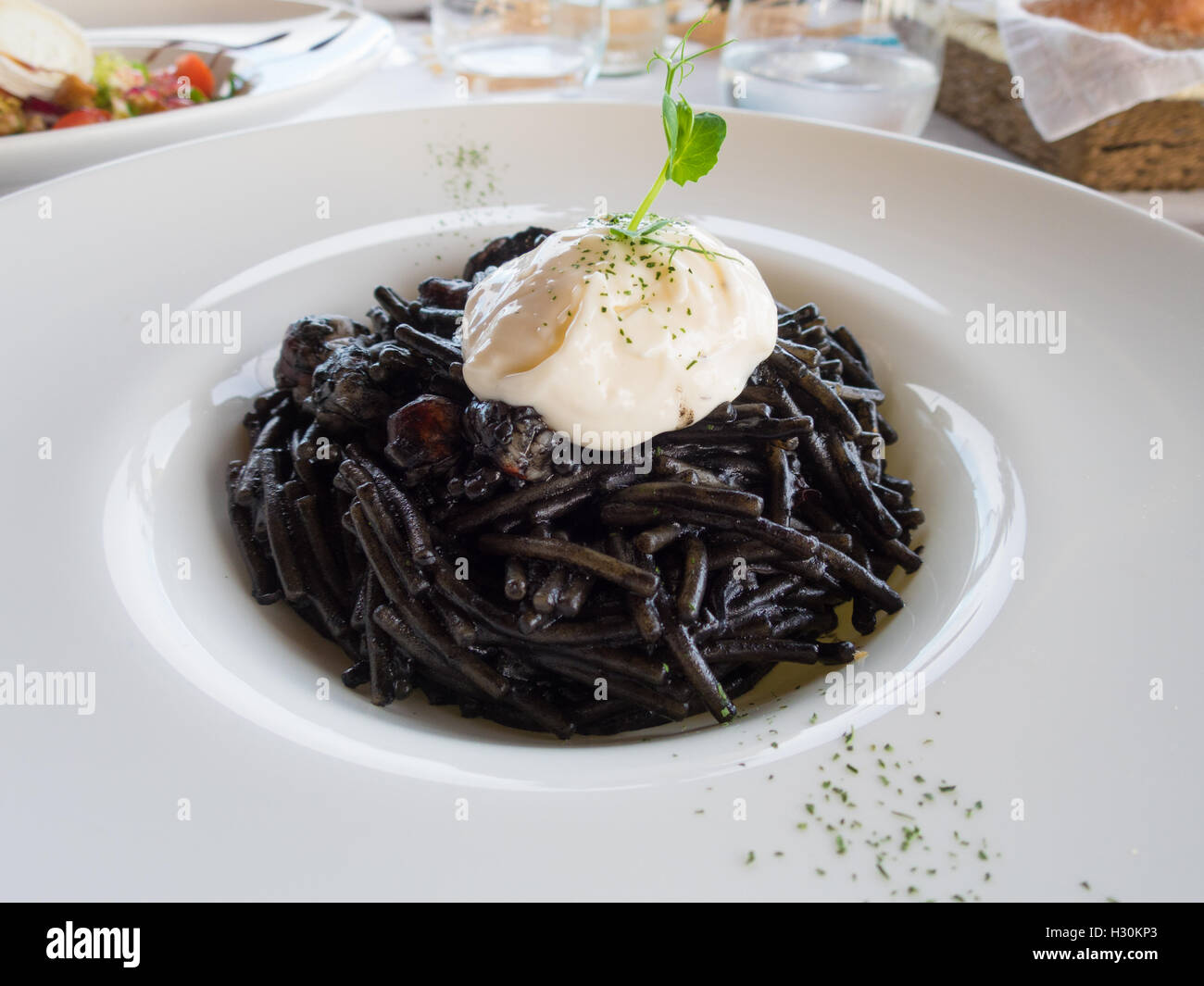 elegant white circular bowl plate with fideua, black ink squid noodles ...