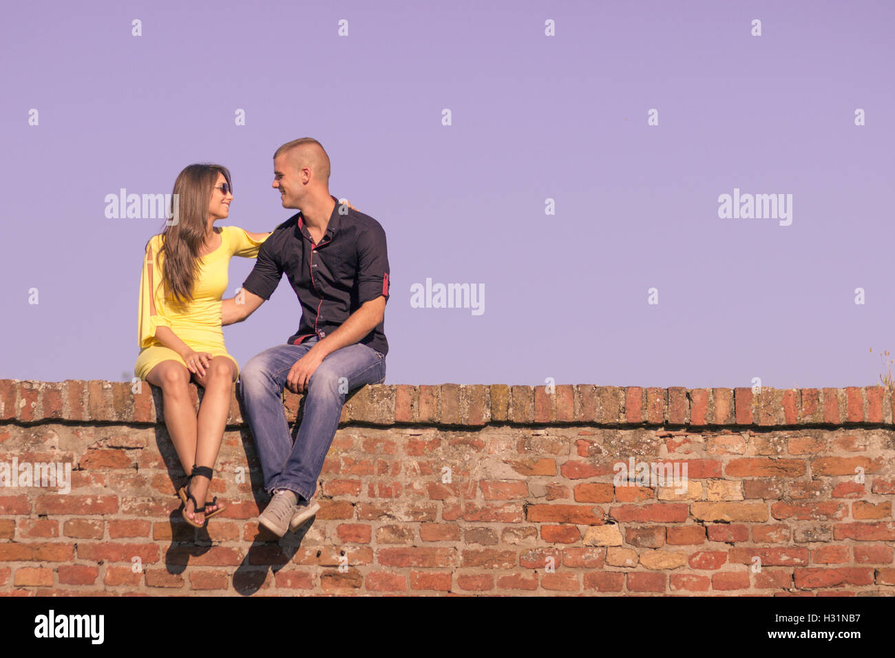 young adult 20s couple hugging sitting brick wall copy space sky ...