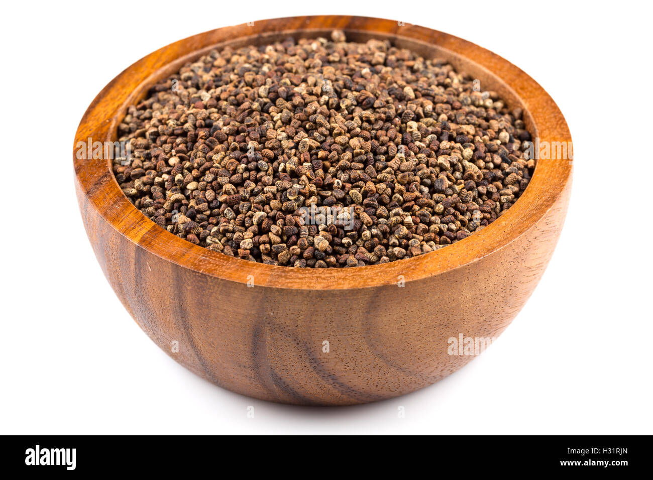 Decorticated cardamom seeds in a dark stone bowl on white background ...