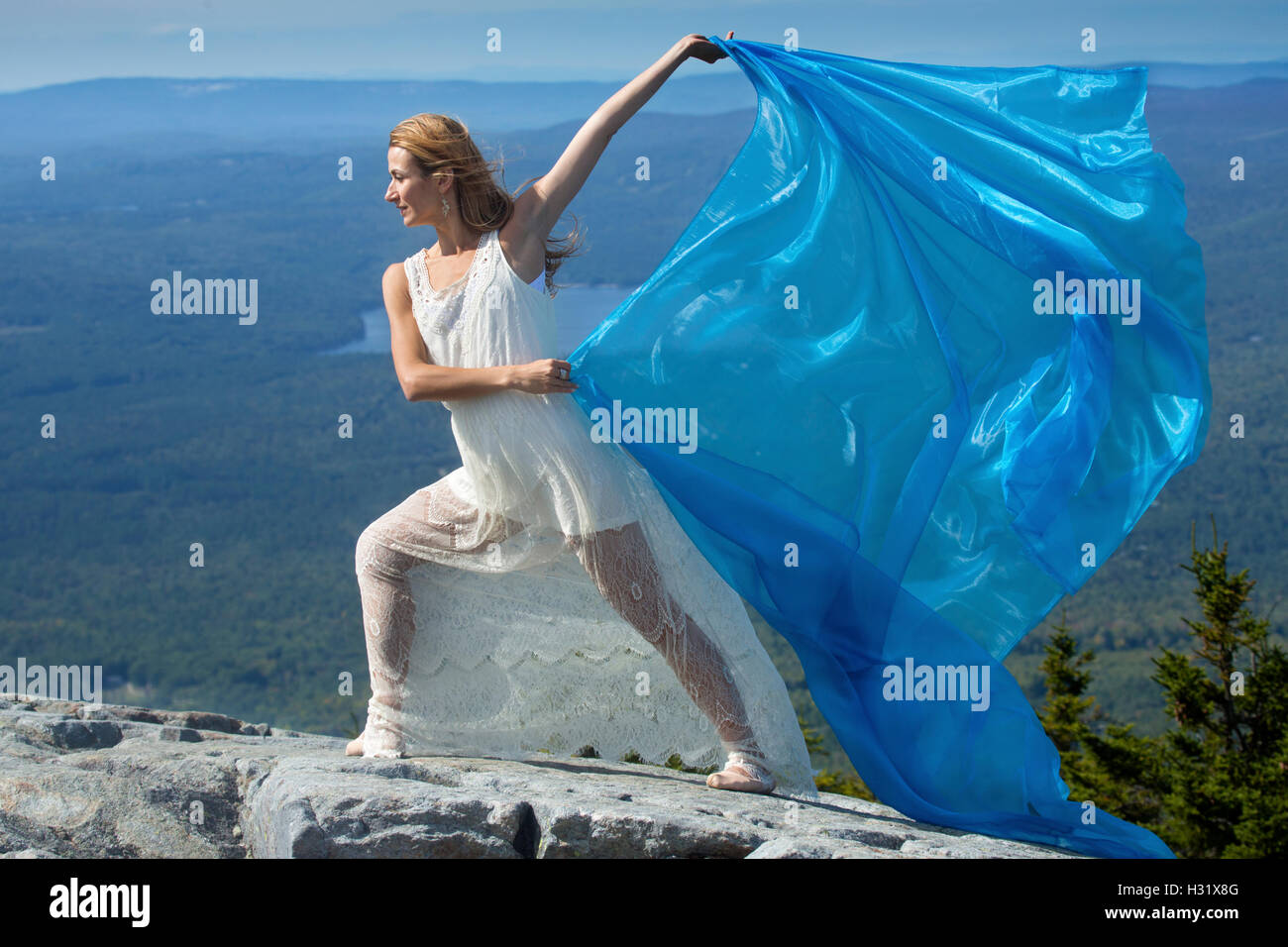 Female dancer in white dress dancing with blue fabric in the wind on ...