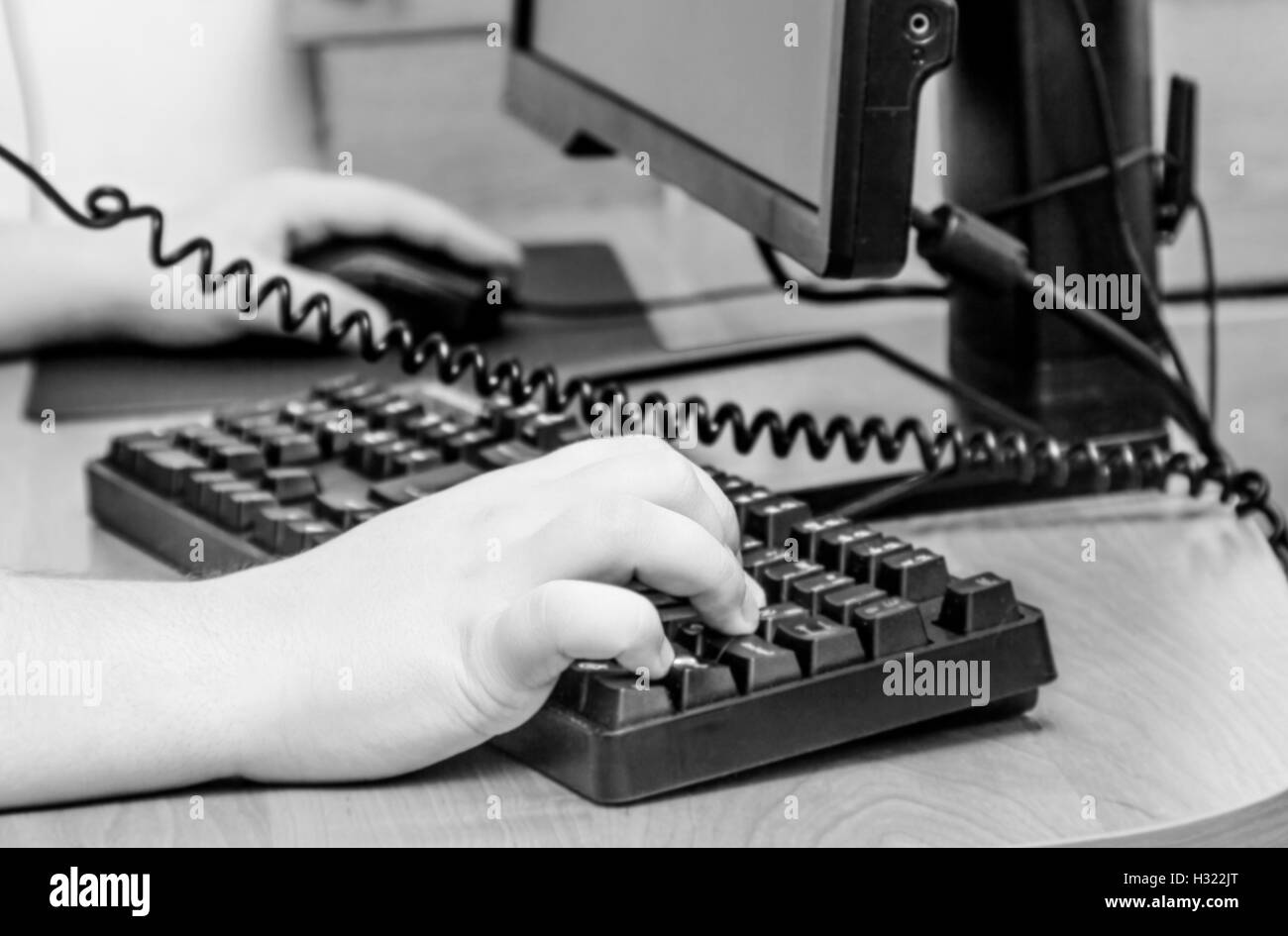 Hands on computer keyboard on wooden table in black amd white colours ...