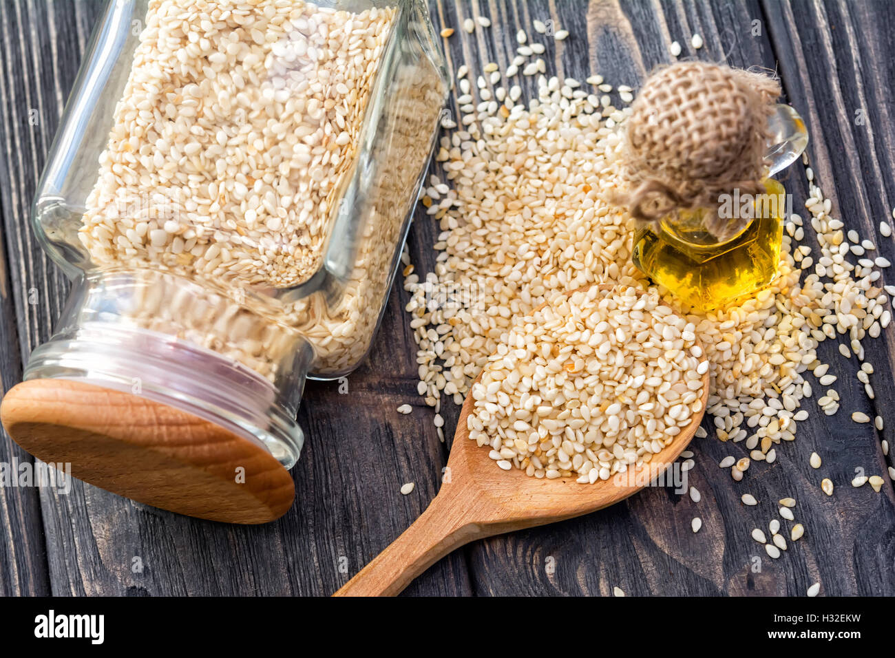 Sesame oil in bottle, sesame seeds in jar, spoon on wooden background ...