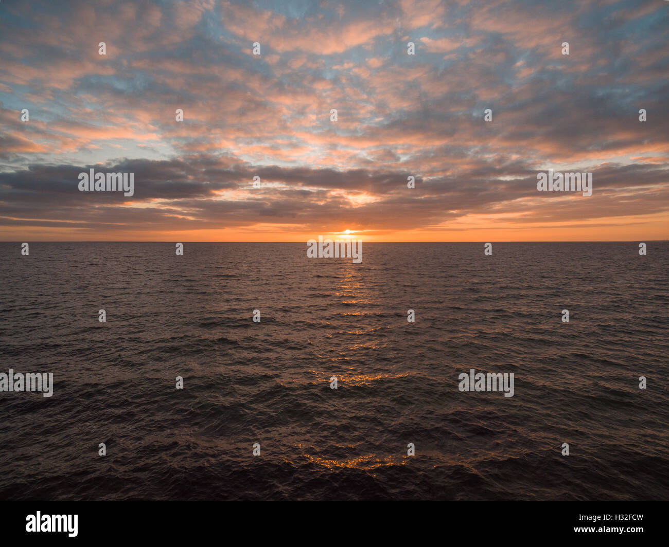 Orange sunset over water with sun peeking out of the clouds Stock Photo ...
