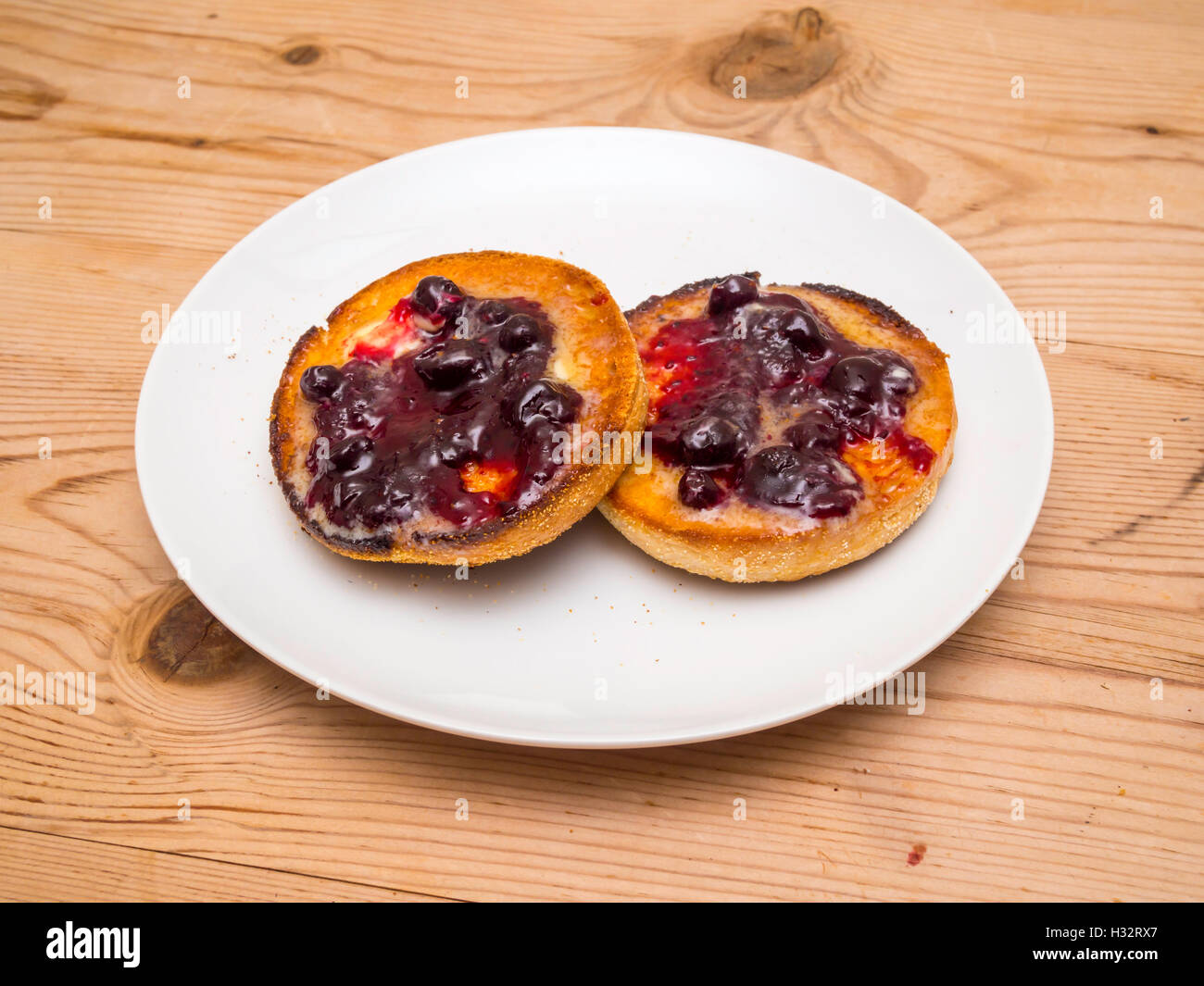 An English Muffin cut in half toasted buttered with blackcurrant jam on ...