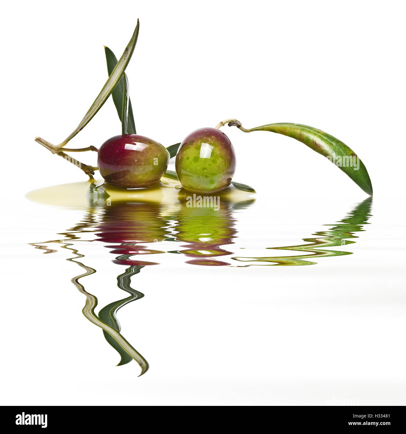 Green olives with leaves covered in olive oil and reflected on water ...