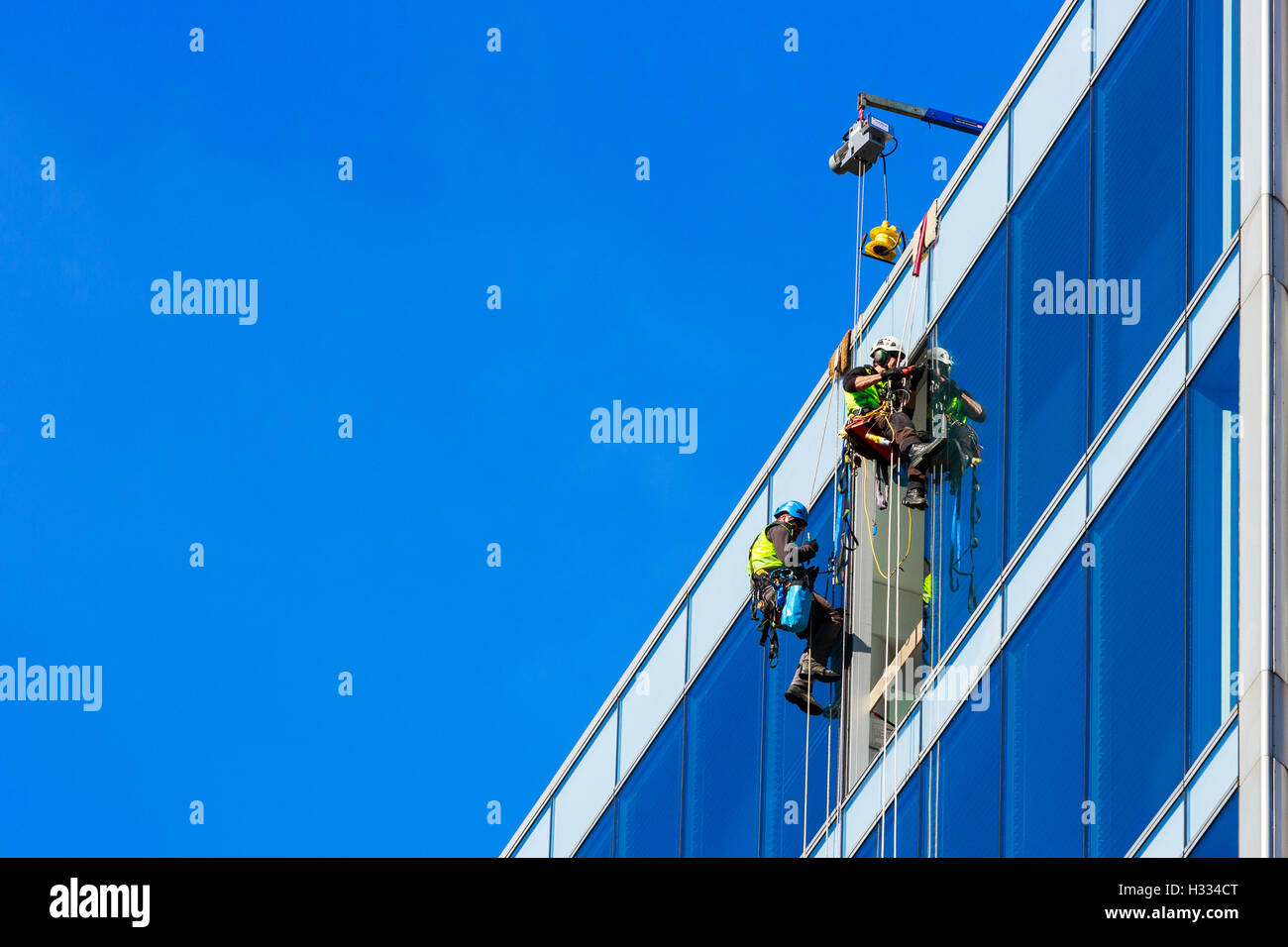 Two workmen repairing window on a tall building while suspended by ...
