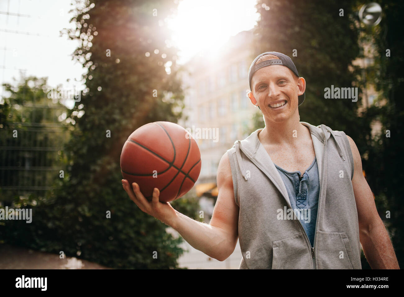 Portrait of smiling young man holding a basketball on outdoor court ...