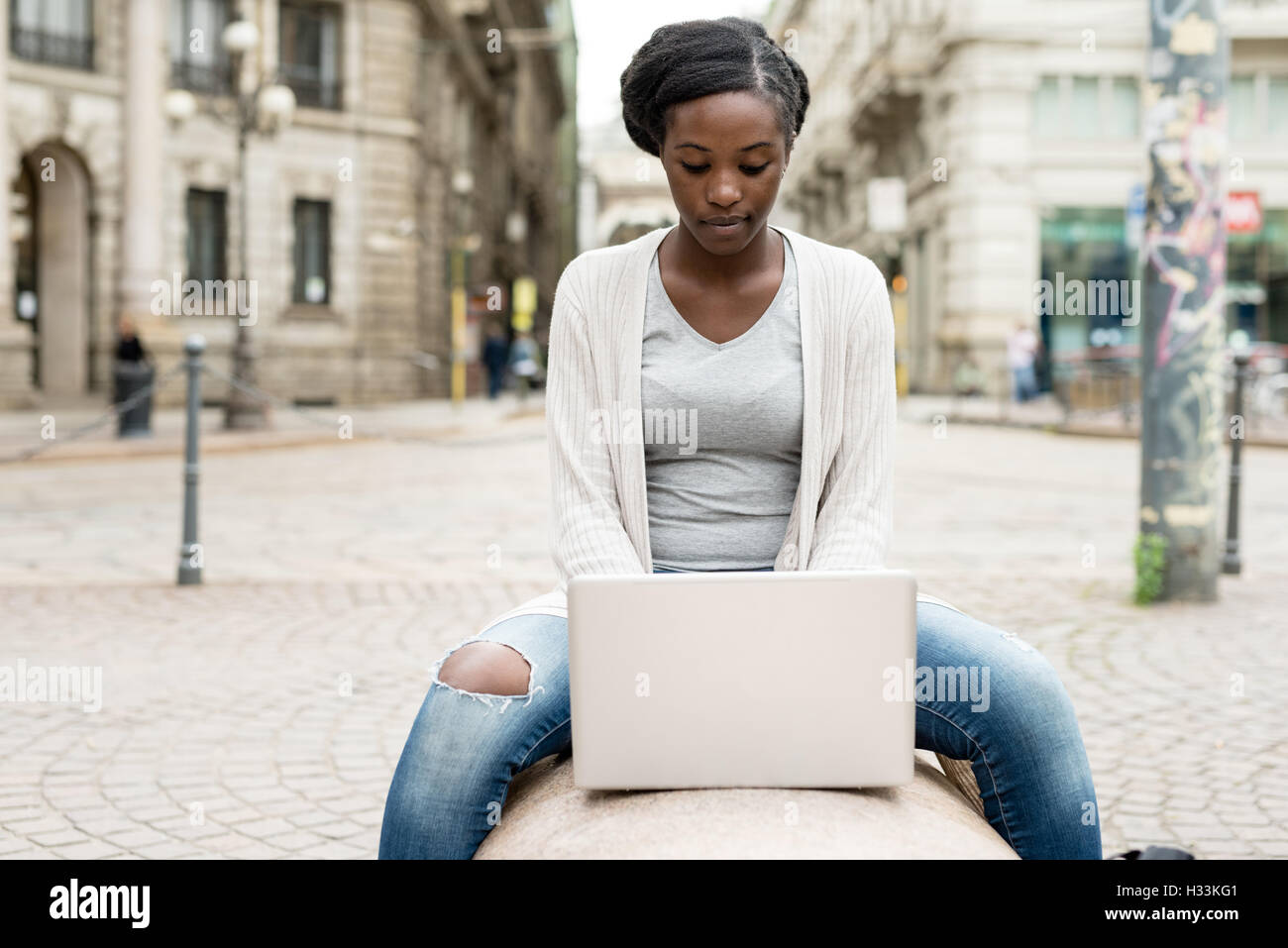 Young black woman using computer outdoor in the city sitting on a bench ...