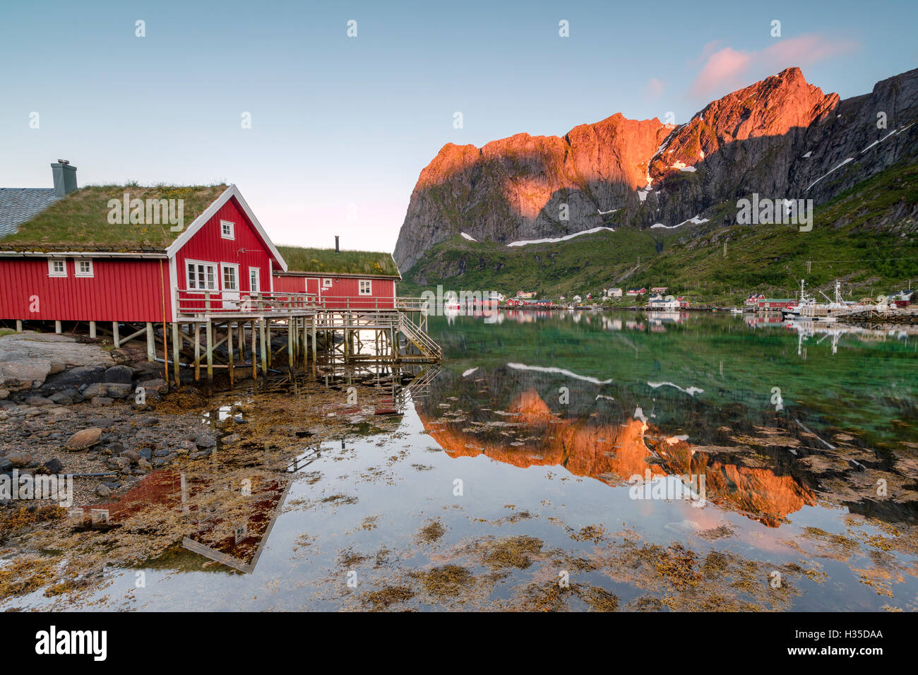 Fishing village and peaks reflected in water under midnight sun, Reine ...