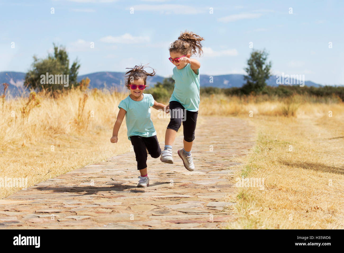 Portrait of little girls in similar wear jumping holding hand in hand ...
