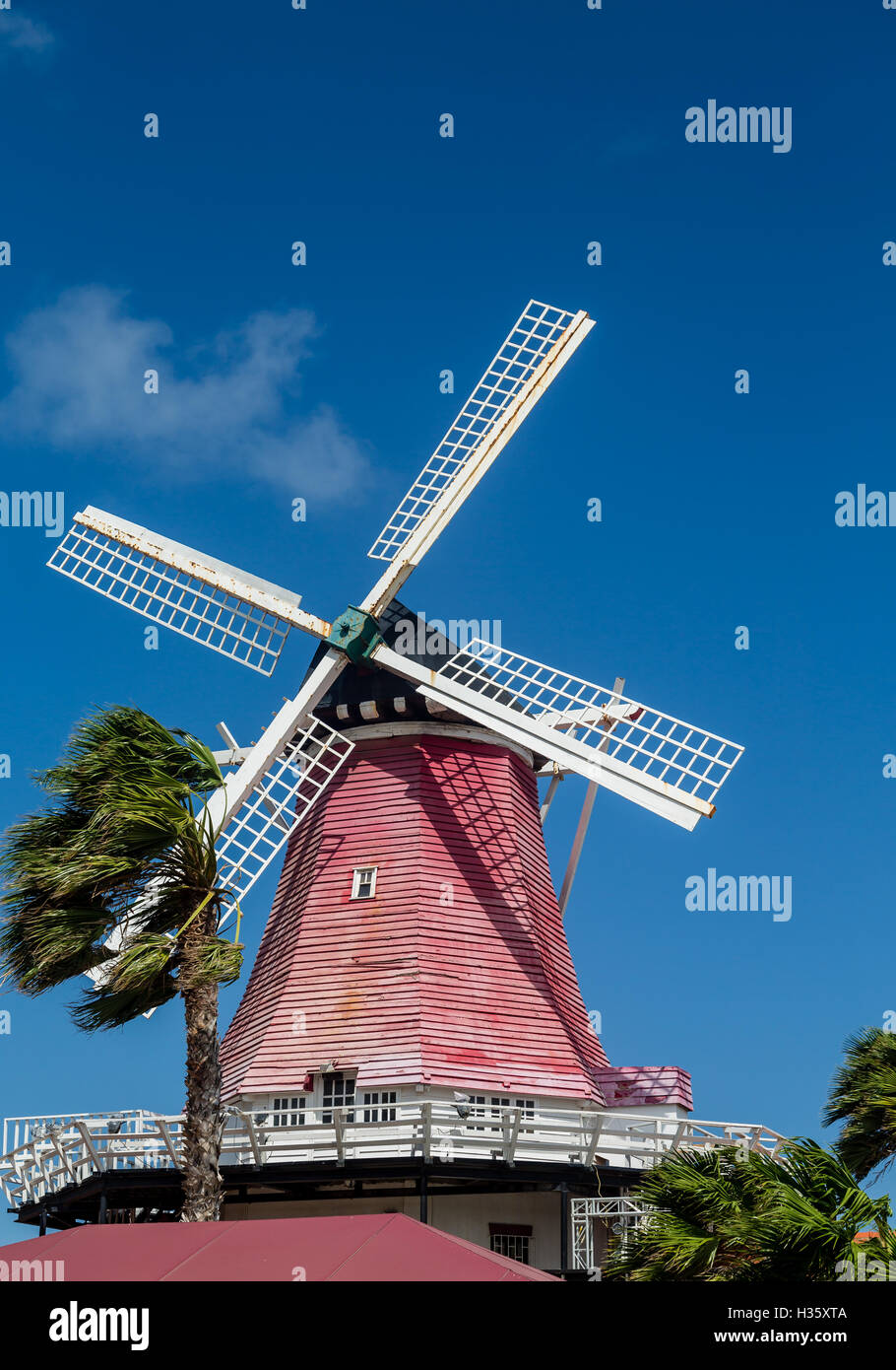 A red windmill with white blades againsta blue sky with palm trees ...