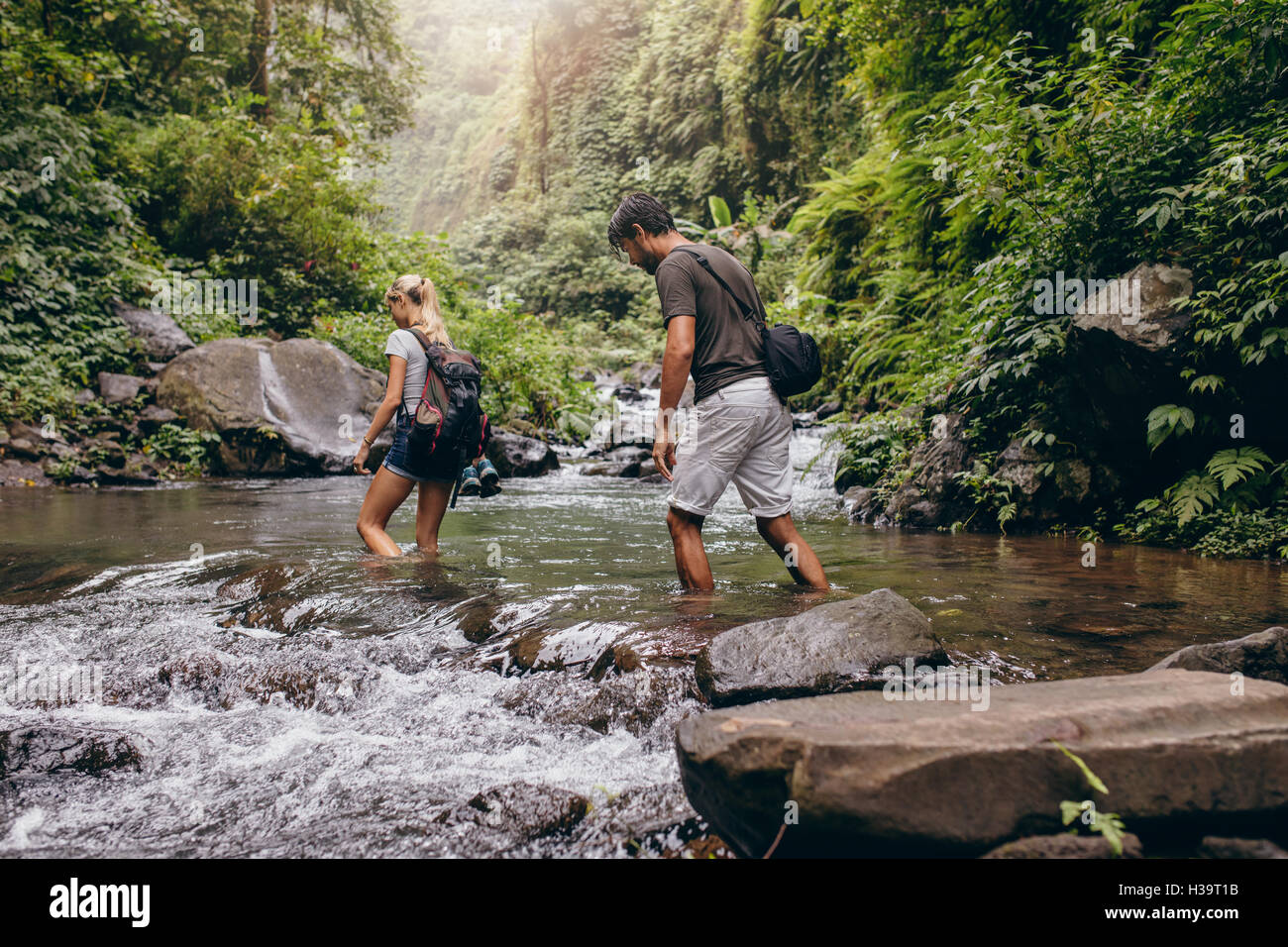 Shot of young man and woman crossing a river during forest hike. Couple ...