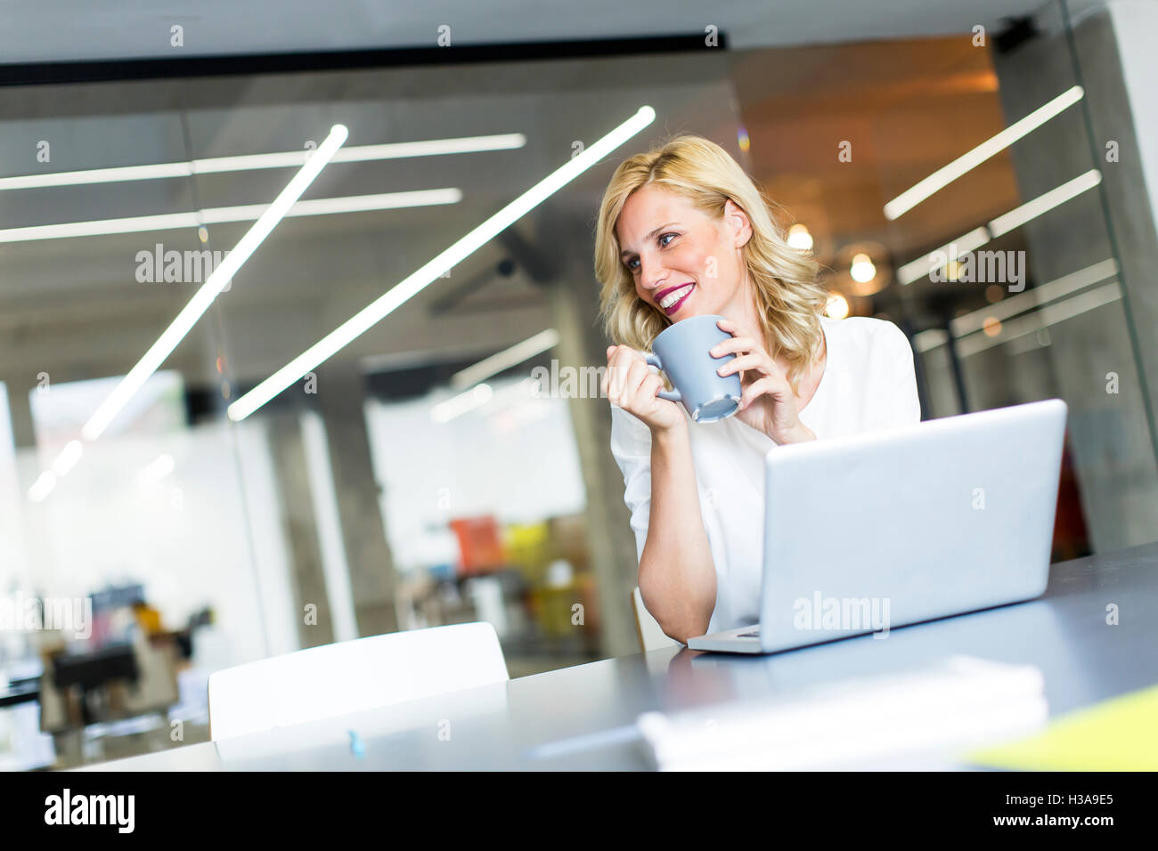 Young woman drinking coffee at the office Stock Photo - Alamy