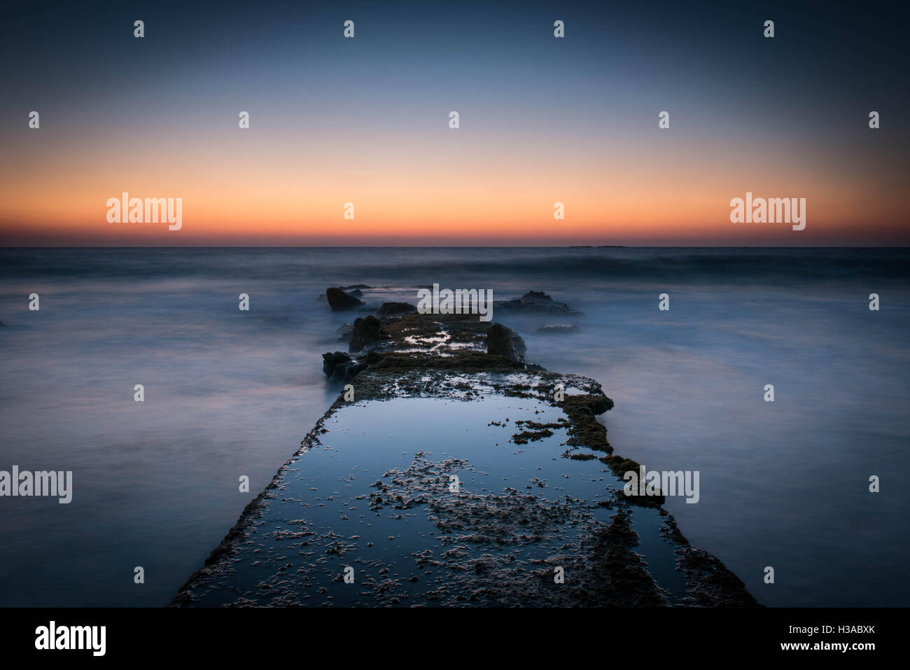 A rocky path into the sea at sunset Stock Photo - Alamy