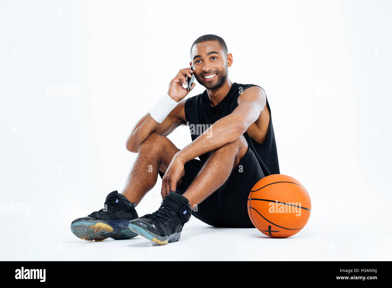 Happy young man basketball player sitting and talking on cell phone ...
