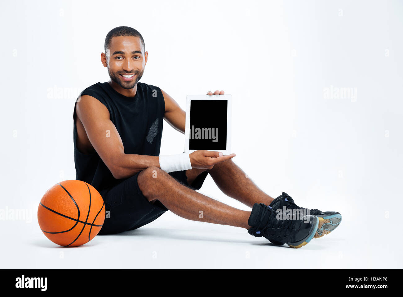 Happy young man basketball player sitting and holding blank screen ...