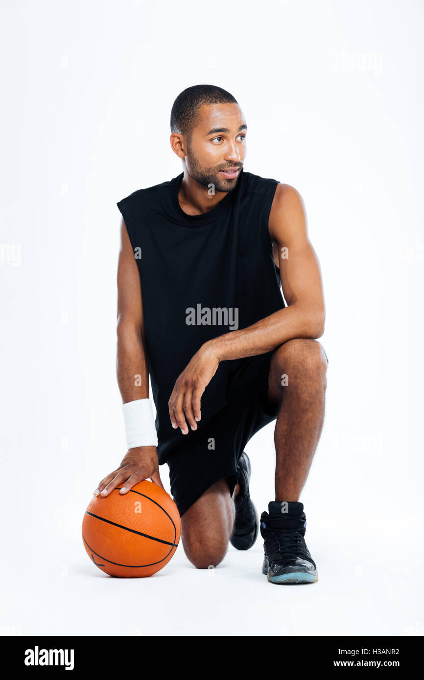 Portrait of attractive young man basketball player standing on one knee ...