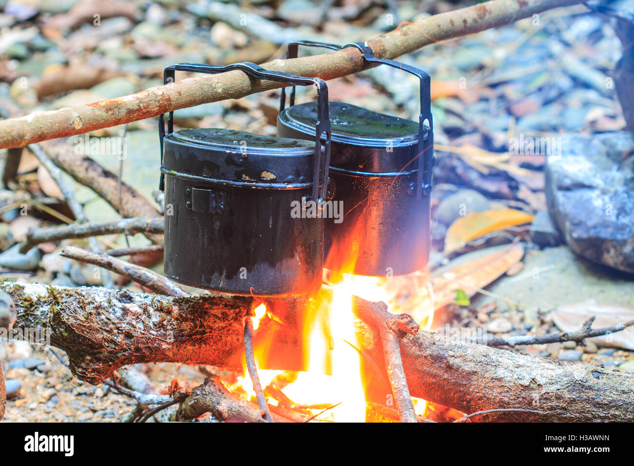 Rice cooking with army pot on bonfire with orange flames and firewood ...