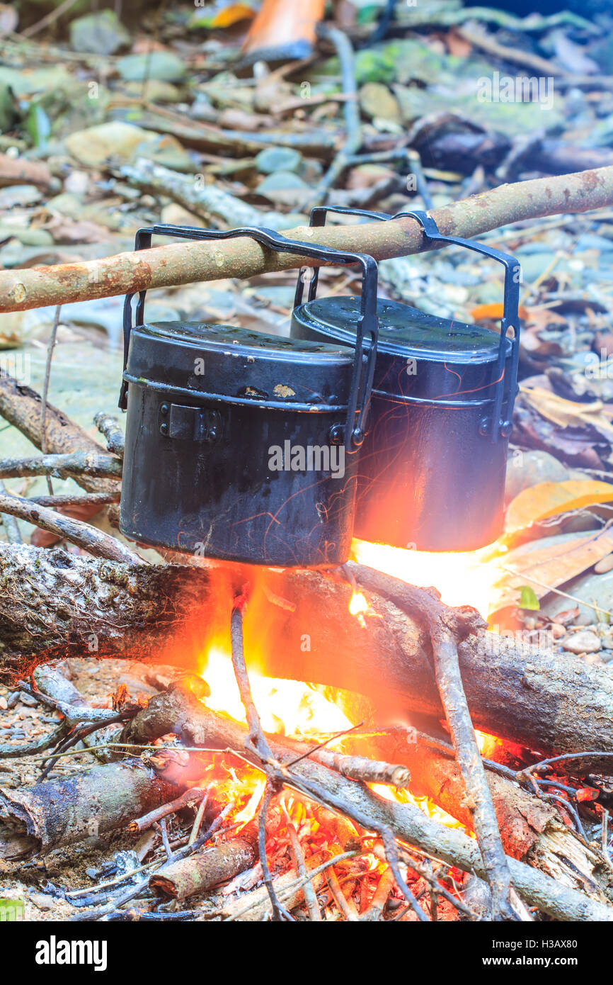 Rice cooking with army pot on bonfire with orange flames and firewood ...