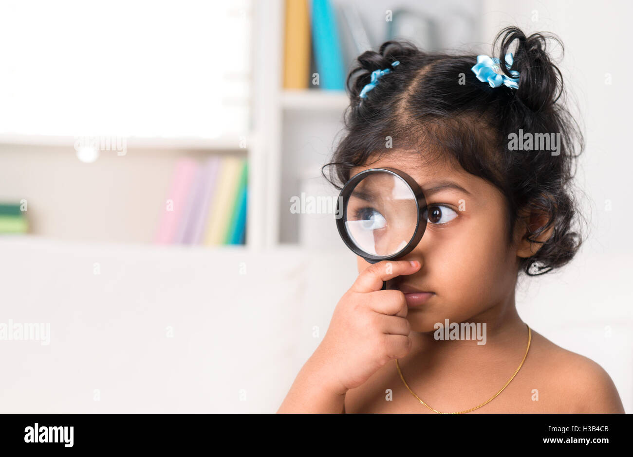 Cute Indian girl peeking through magnifying glass Stock Photo - Alamy