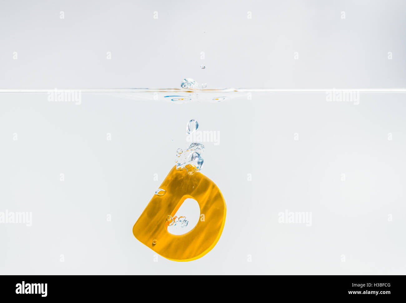 Yellow wooden alphabet D drop in the water with white background and ...