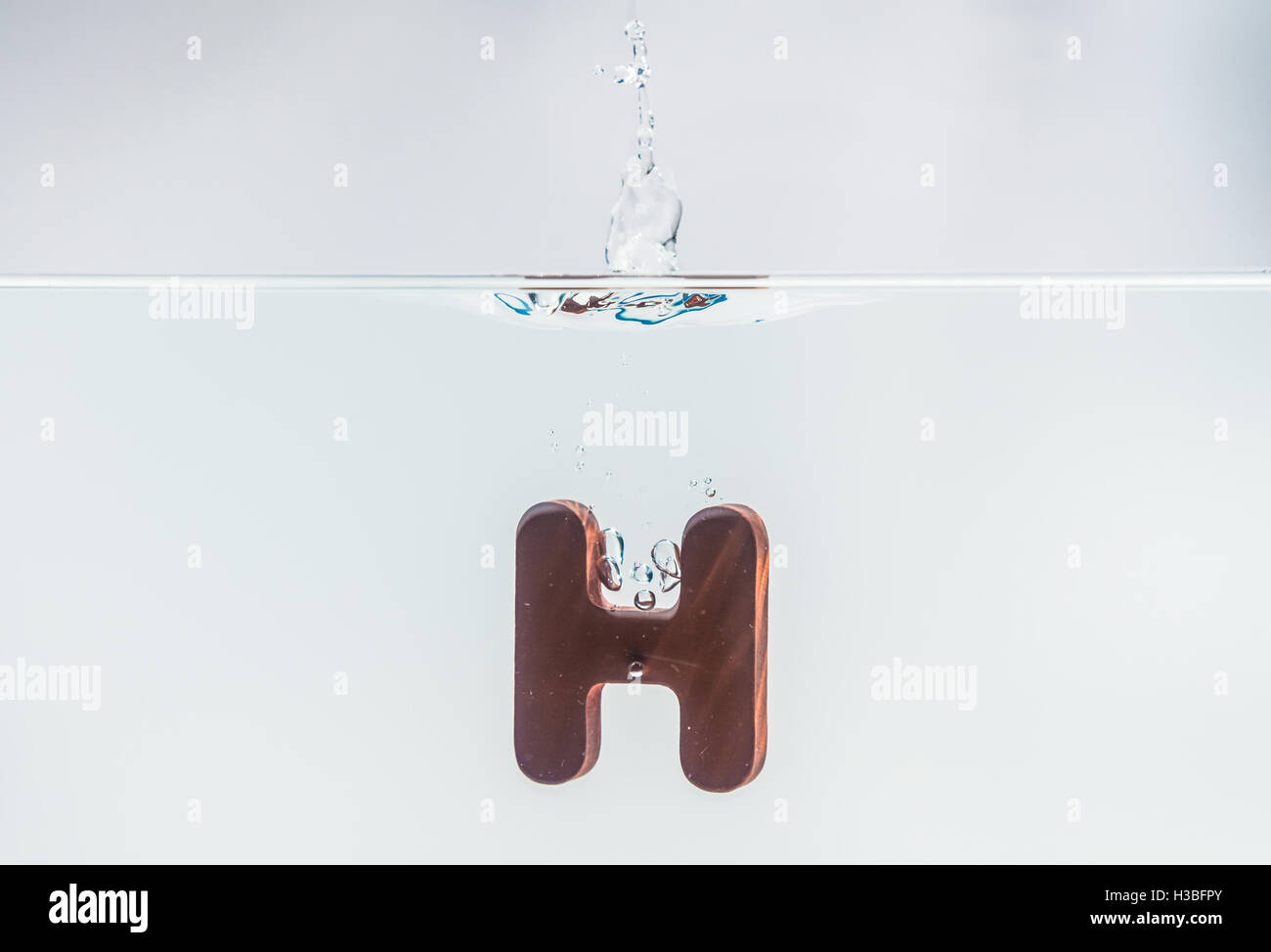 Brown wooden alphabet H drop in the water with white background and ...