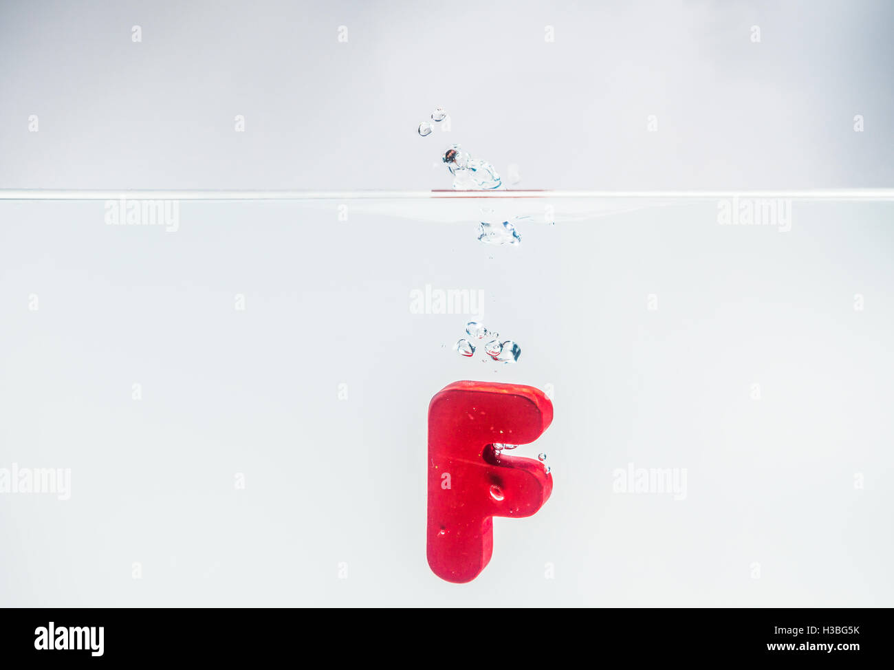 Red wooden alphabet F drop in the water with white background and ...