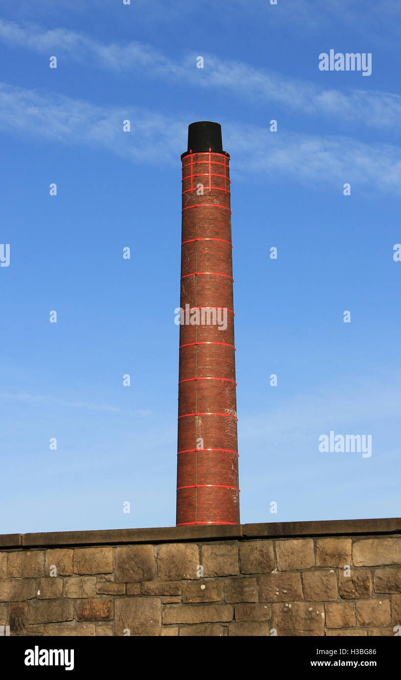 A former textile mill chimney stretches into a blue sky above ...