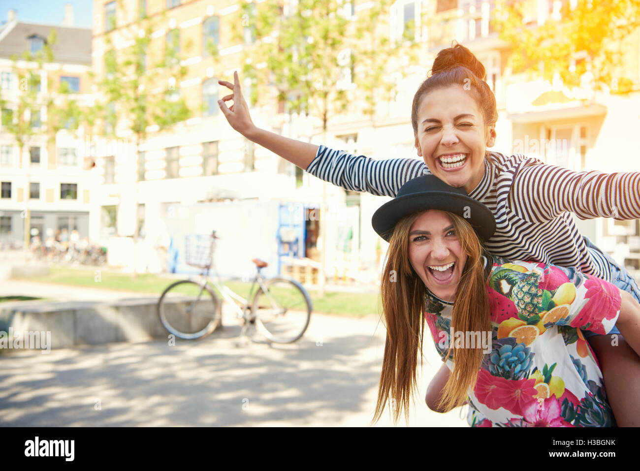 Laughing young female friends piggy back riding outdoors on a ...