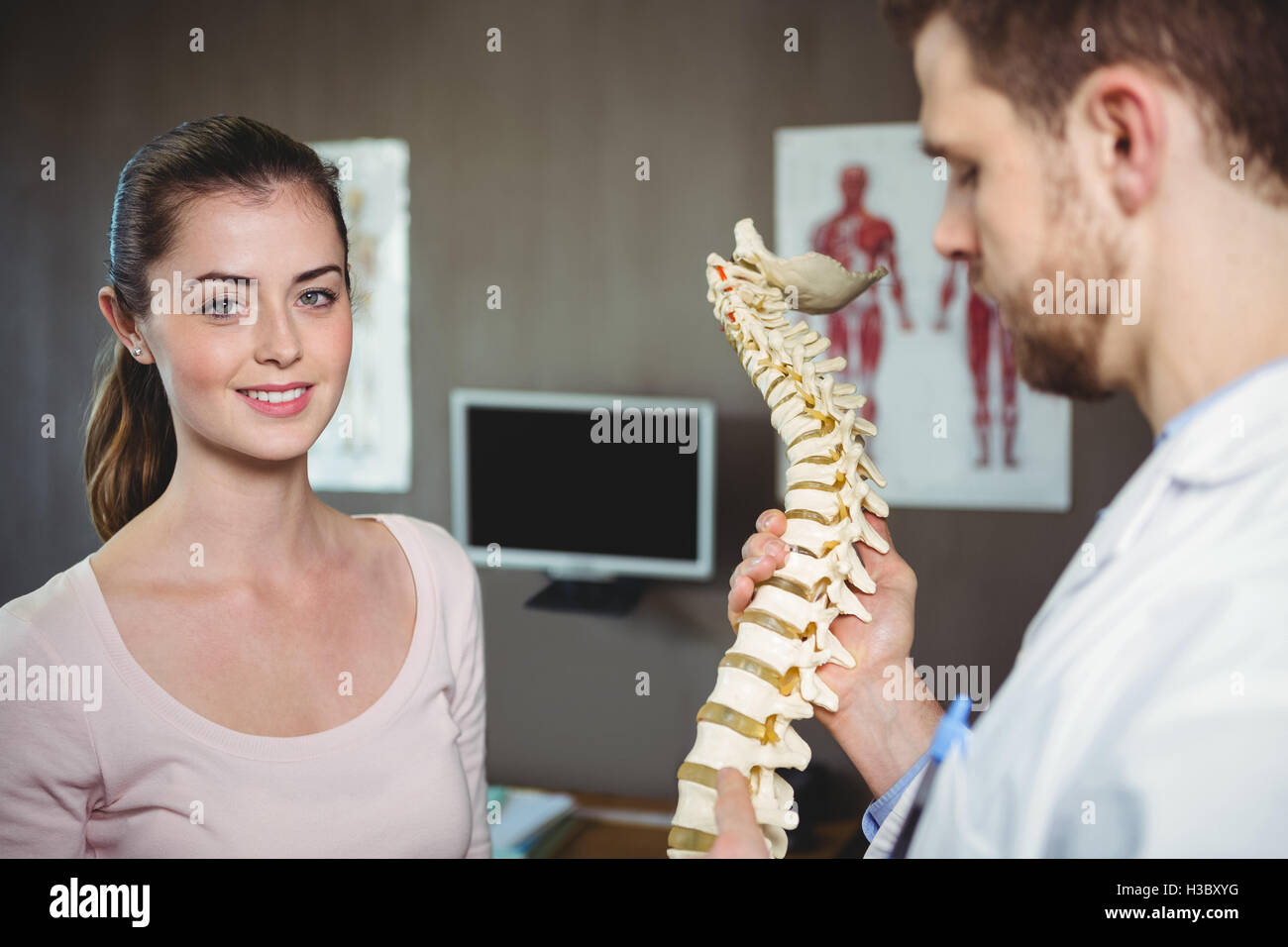 Physiotherapist holding spine model while patient smiling at camera ...