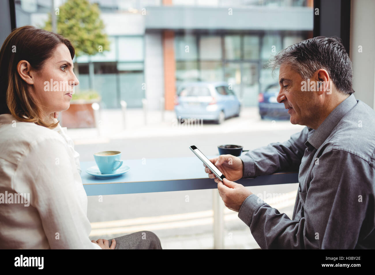 Man using mobile phone while talking with woman Stock Photo - Alamy