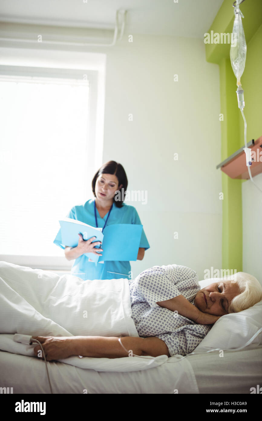 Senior patient sleeping on a bed while nurse checking report Stock ...