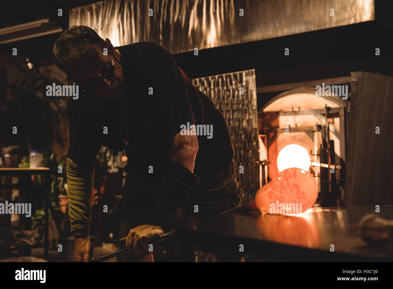 Glassblower shaping a molten glass on a marver table Stock Photo - Alamy